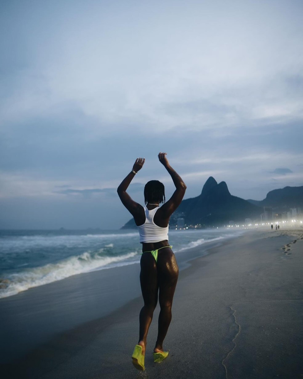 Rebecca posa em praia paradisíaca com peças em neon